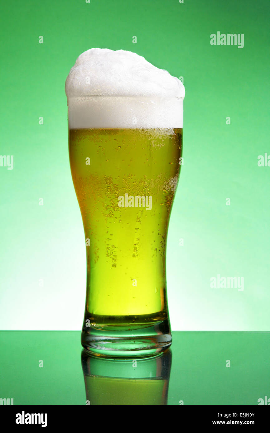 Glass of beer with froth over green background Stock Photo - Alamy