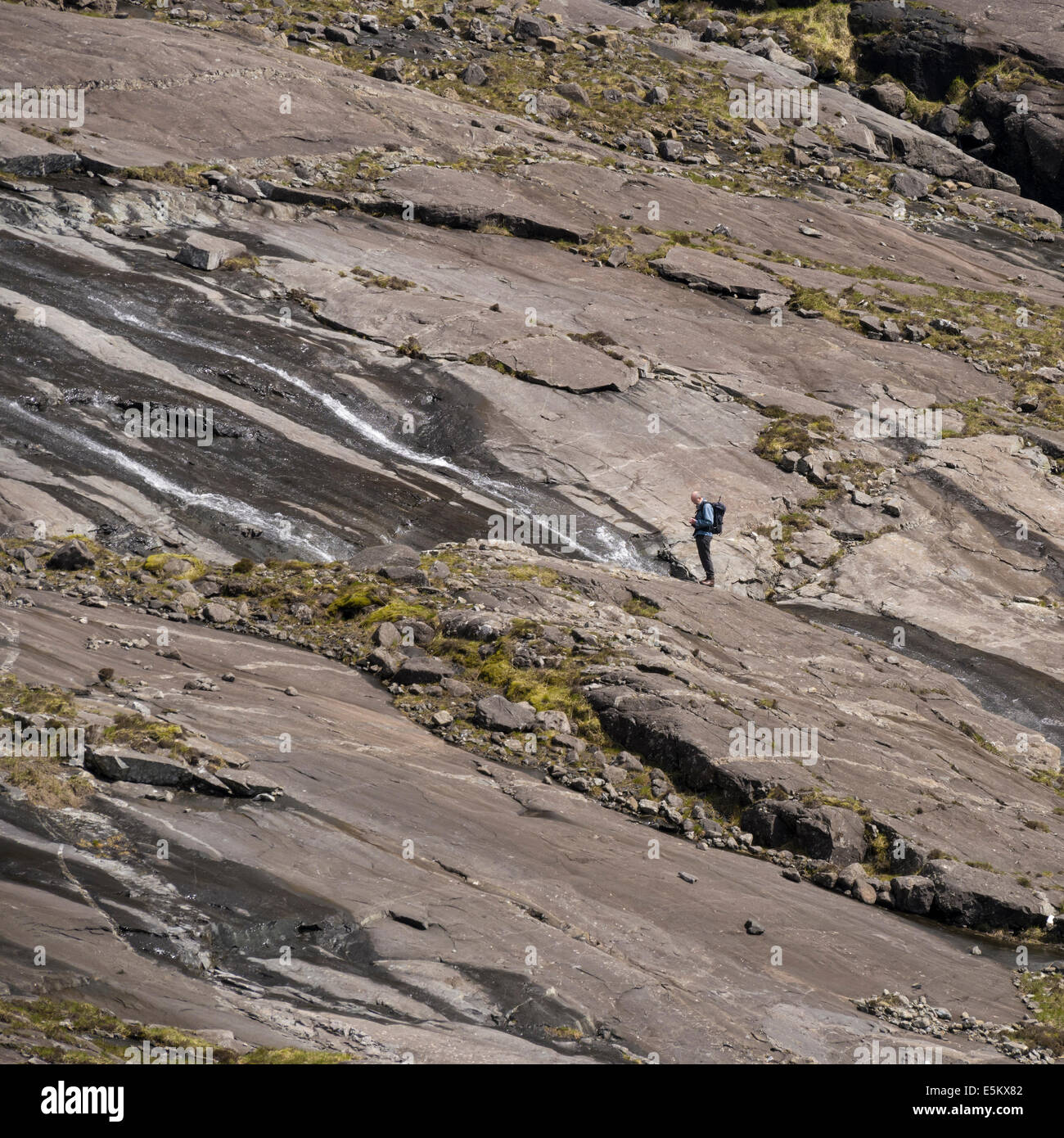 Lone mountain walker on steep rock slabs below Coir' a' Ghrunnda in the ...