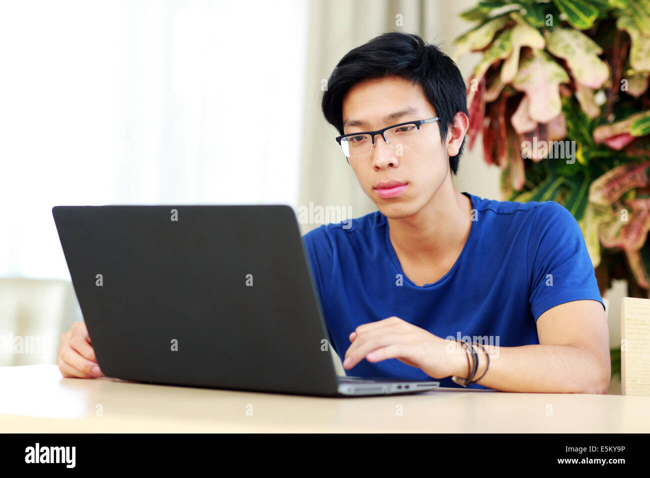 Serious asian man sitting at the table and using laptop Stock Photo - Alamy