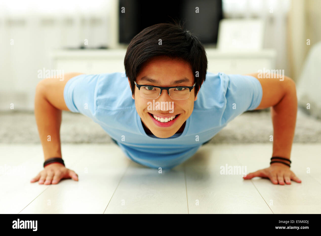 Portrait of a happy young man doing push ups in the living room at home ...