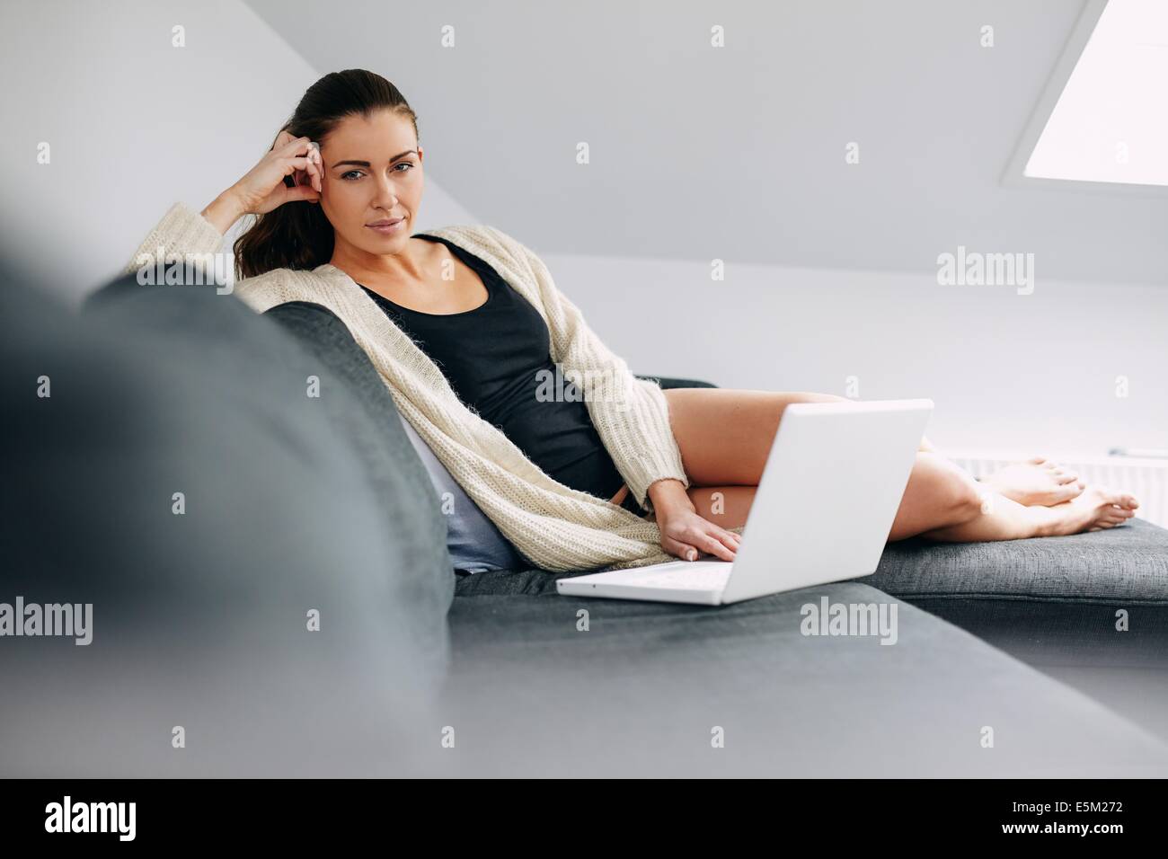 Portrait of attractive young woman with a laptop sitting on a couch ...