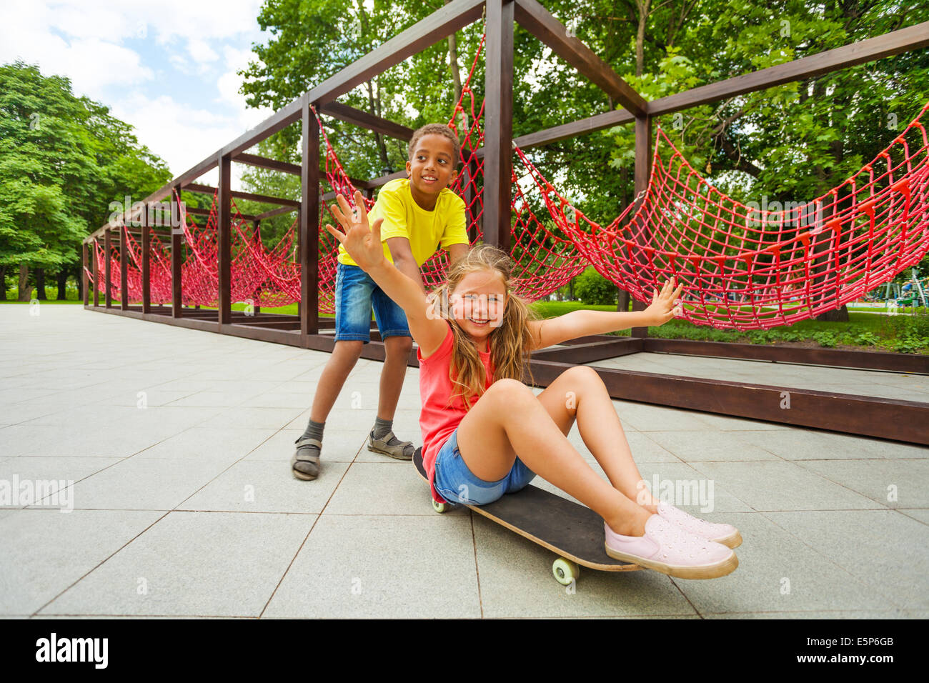Boy pushing girl sitting on skateboard and roll Stock Photo - Alamy