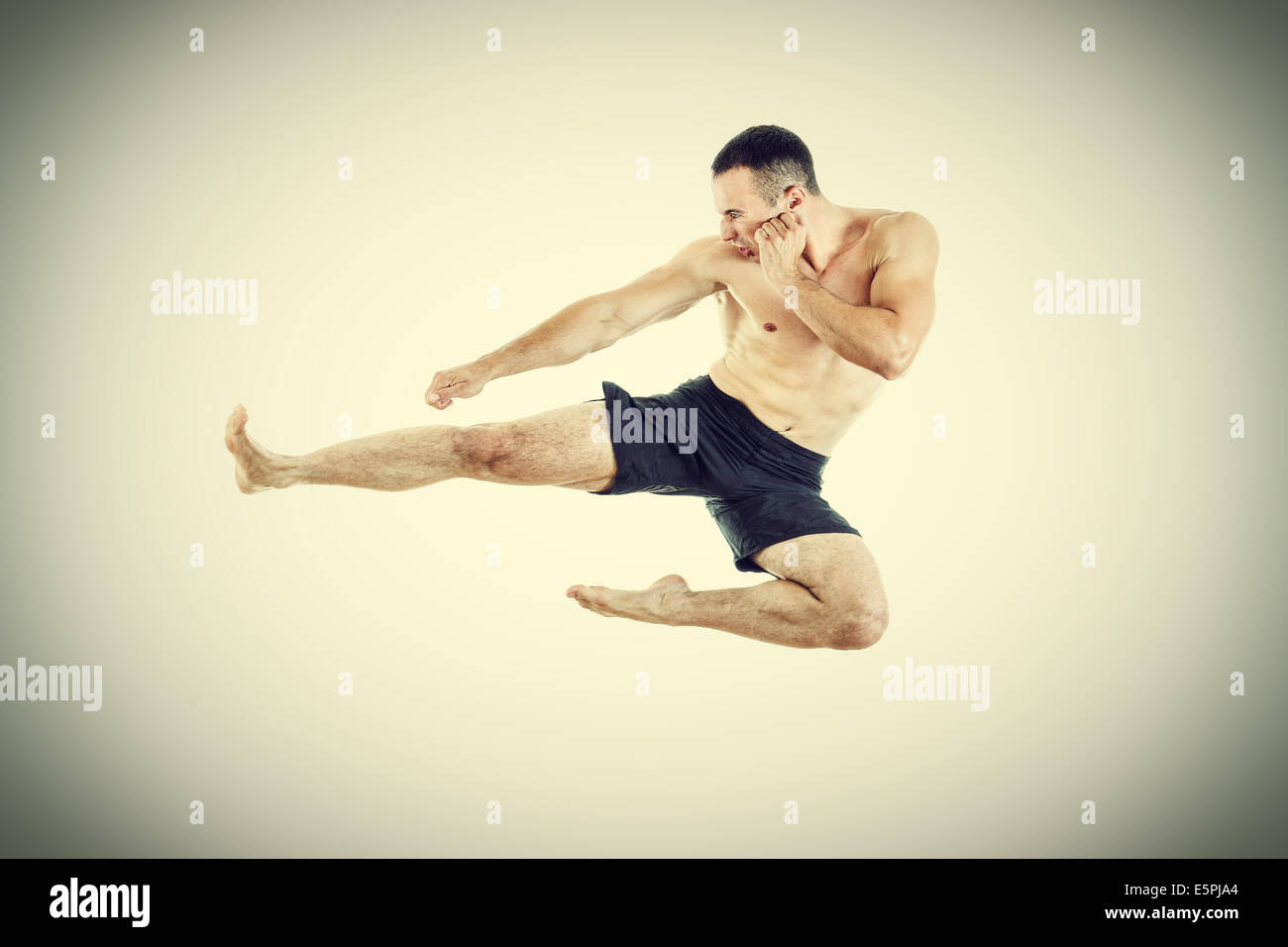 Determined muscular fighter performing professional flying kick in full ...