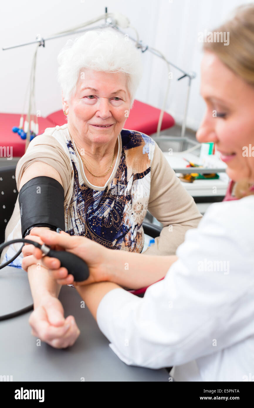 Young female doctor measuring blood pressure of senior patient in ...