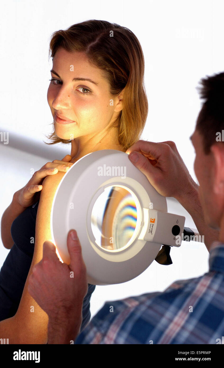 Dermatologist using a magnifying lens to examine the skin of a patient ...