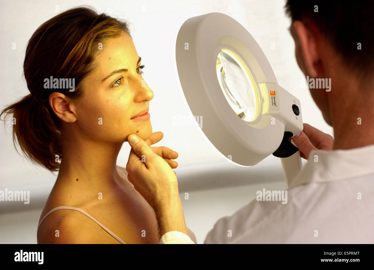 Dermatologist using a magnifying lens to examine the skin of a patient ...