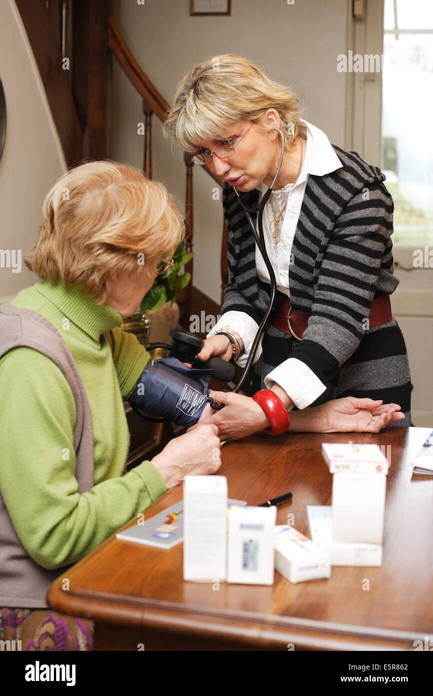 General practitioner checking blood pressure of elderly patient during ...
