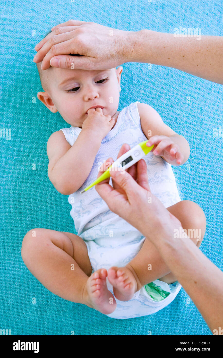 Mother checking the temperature of her 7 month old feverish baby with a ...