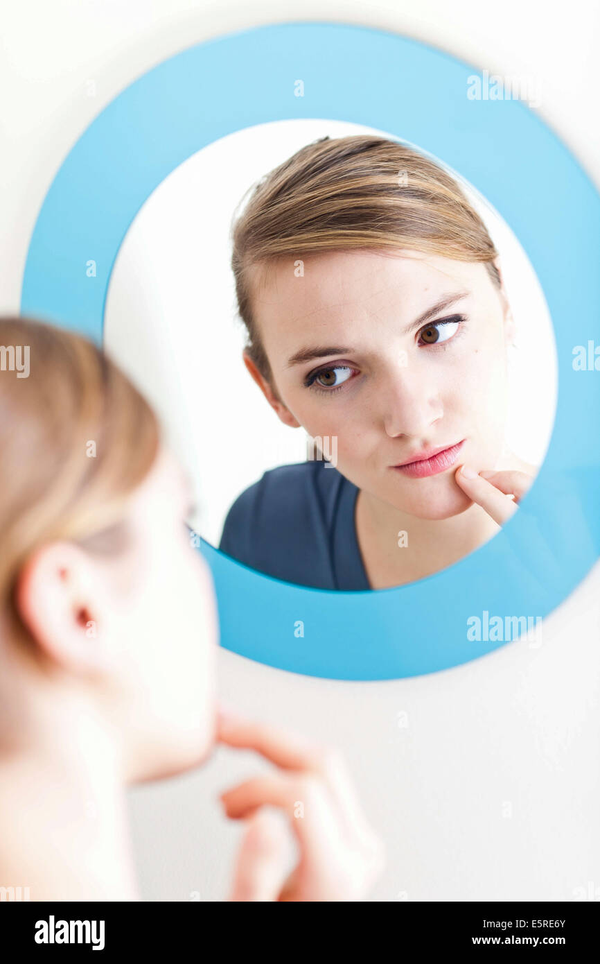 Young woman checking her face in the mirror Stock Photo - Alamy