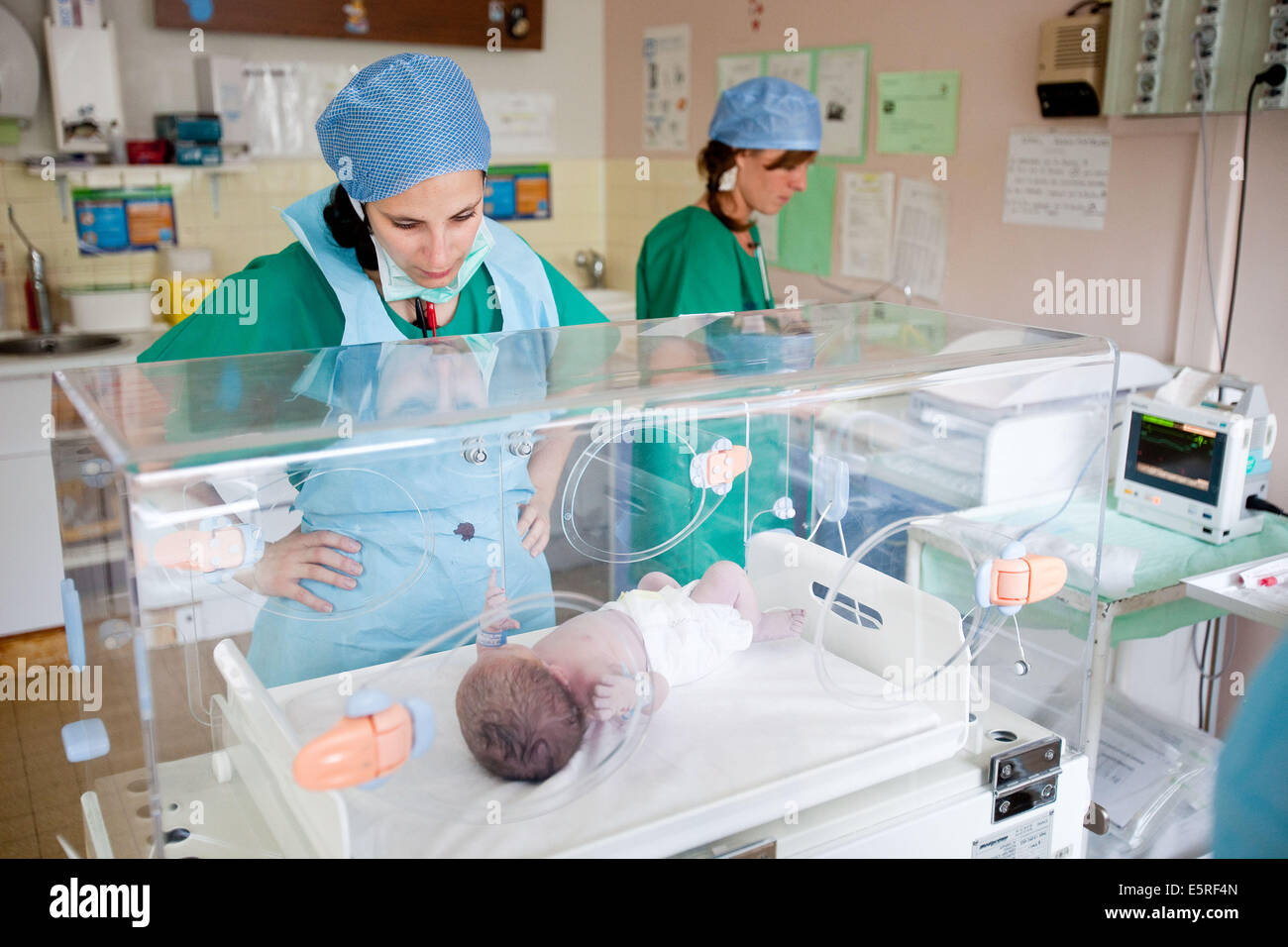Midwife looking at a newborn baby in an incubator, Maternity department ...