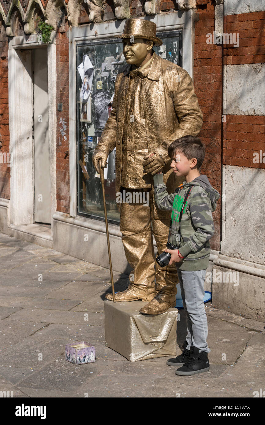 Young boy stands with golden living statue street performer during ...