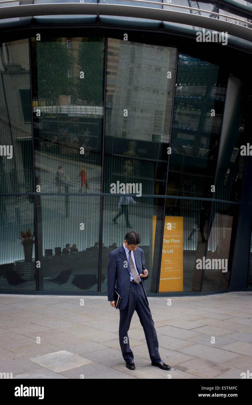 Businessman checks messages beneath modern office entrance architecture ...