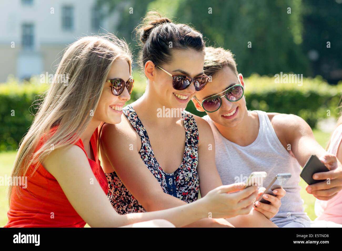 smiling friends with smartphones sitting in park Stock Photo - Alamy