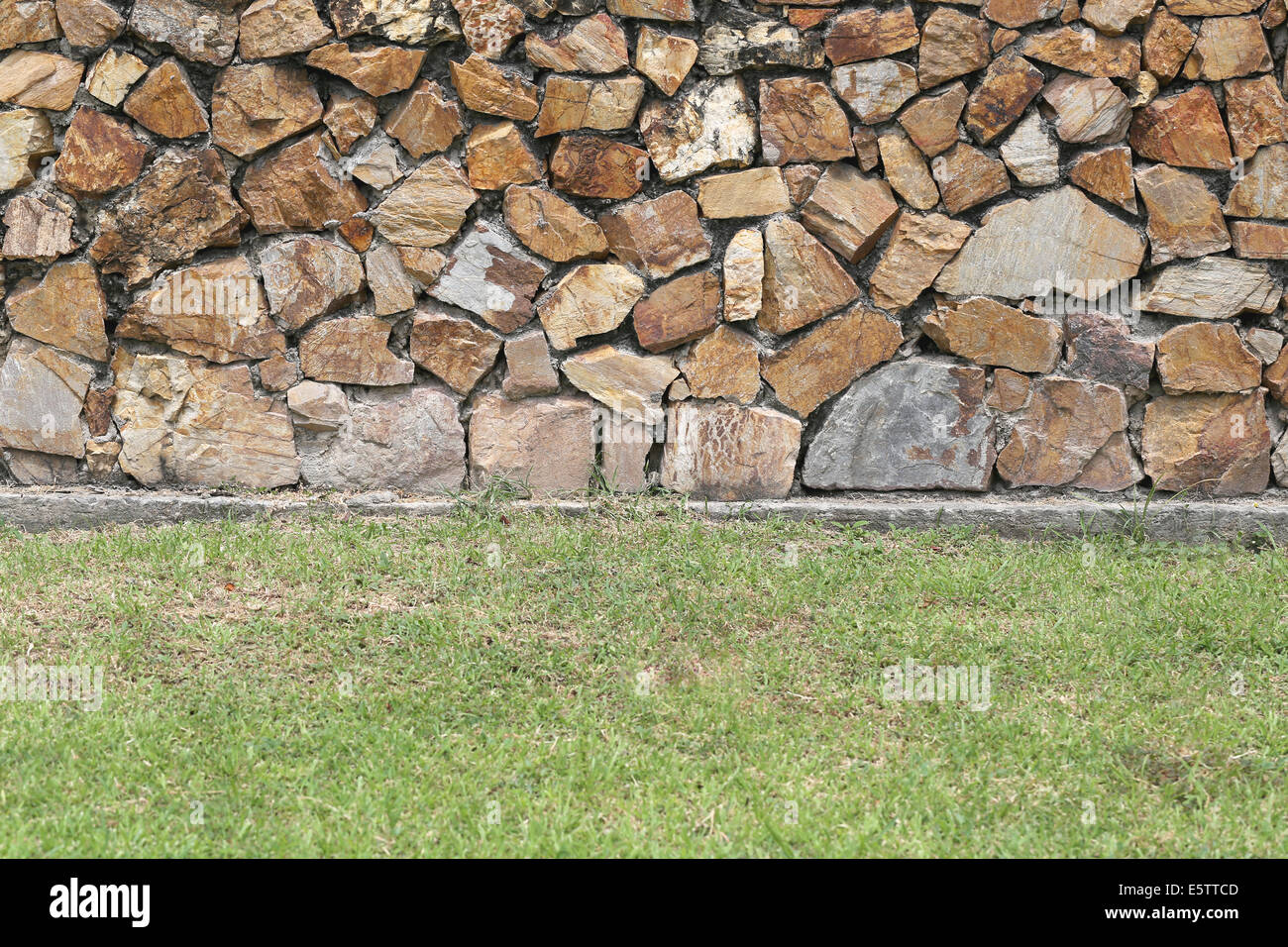 Brown stone wall and green lawn for background Stock Photo - Alamy