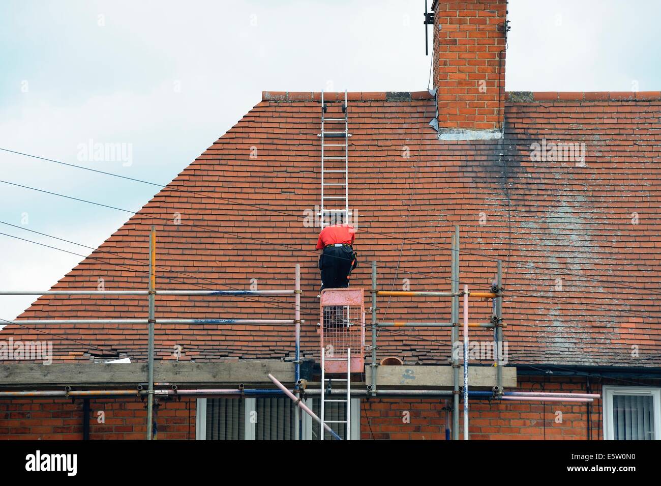 A workman climbing a ladder to repair the top of a roof england uk ...