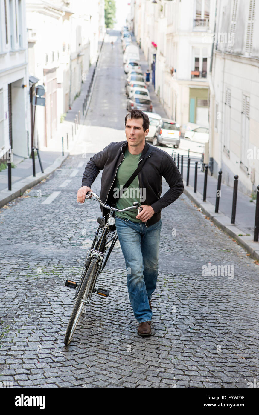 Mid adult man pushing bicycle up cobbled city street Stock Photo - Alamy