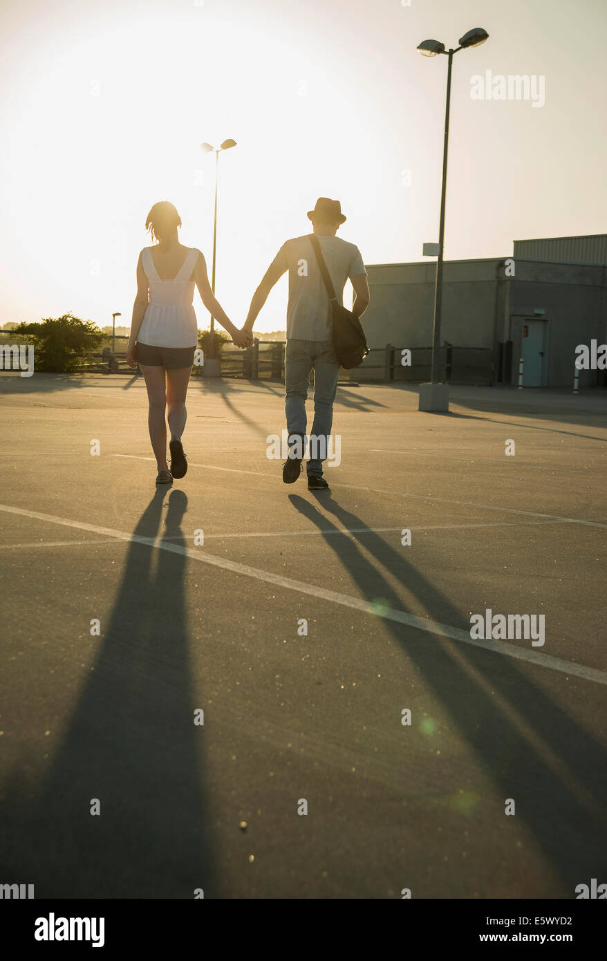 Romantic young couple strolling hand in hand across empty parking lot ...