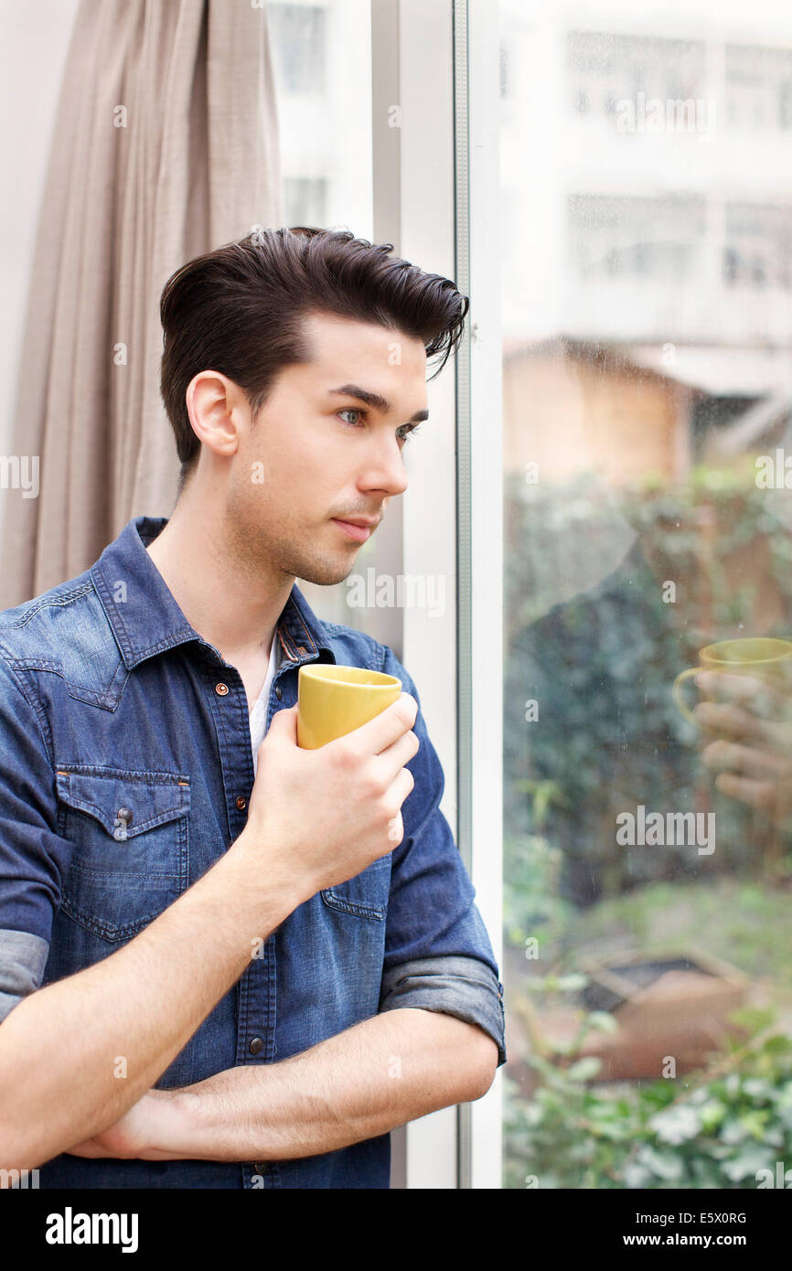 Portrait of young man gazing through patio door Stock Photo - Alamy