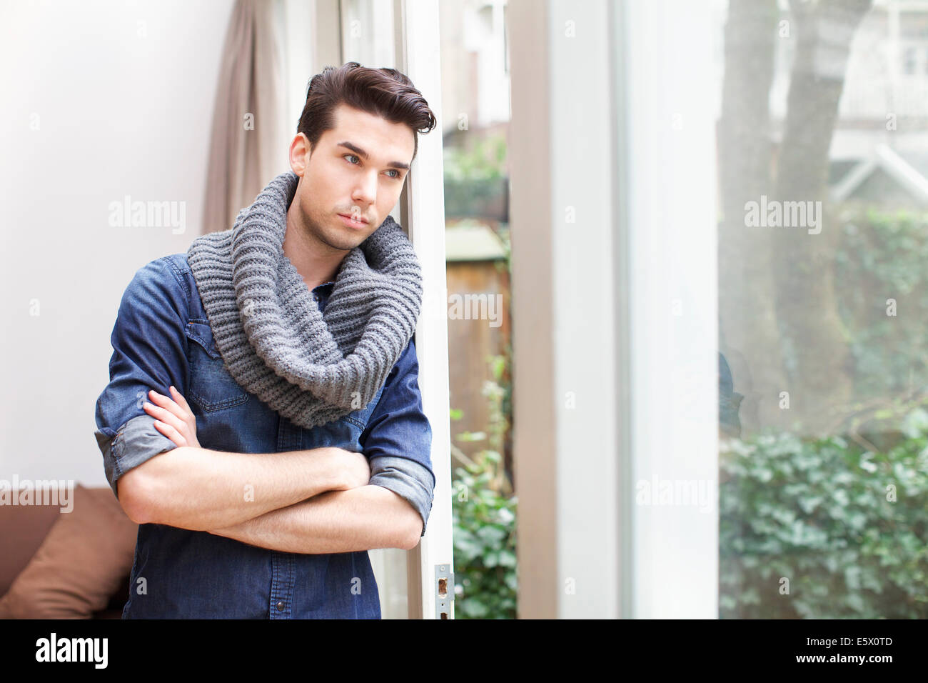 Young man gazing out of window in living room Stock Photo - Alamy