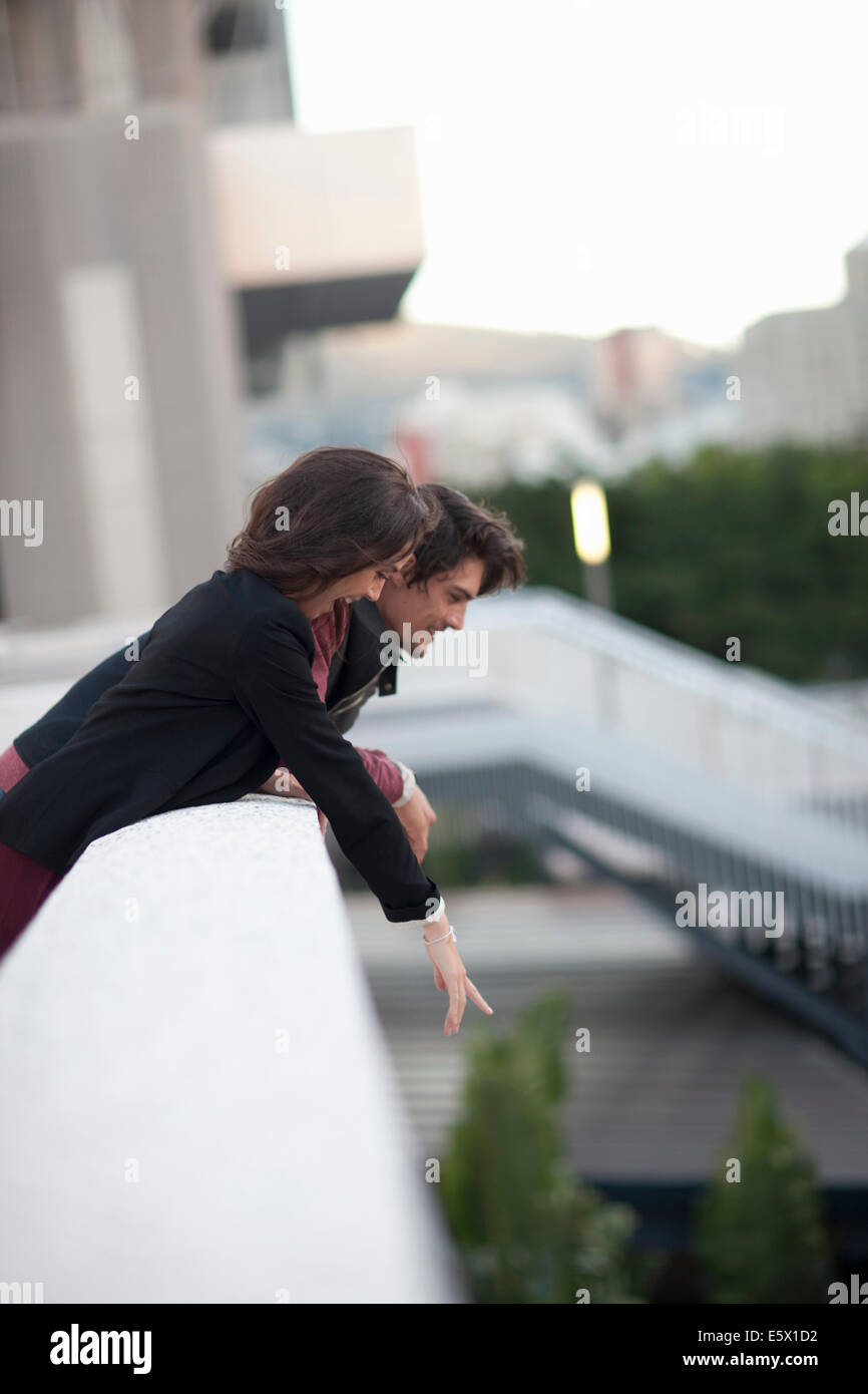 Couple looking down and pointing from city rooftop Stock Photo - Alamy