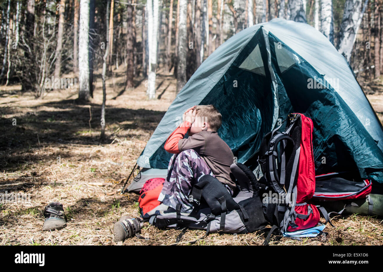 Boy with hands over his face sitting outside tent in forest Stock Photo ...