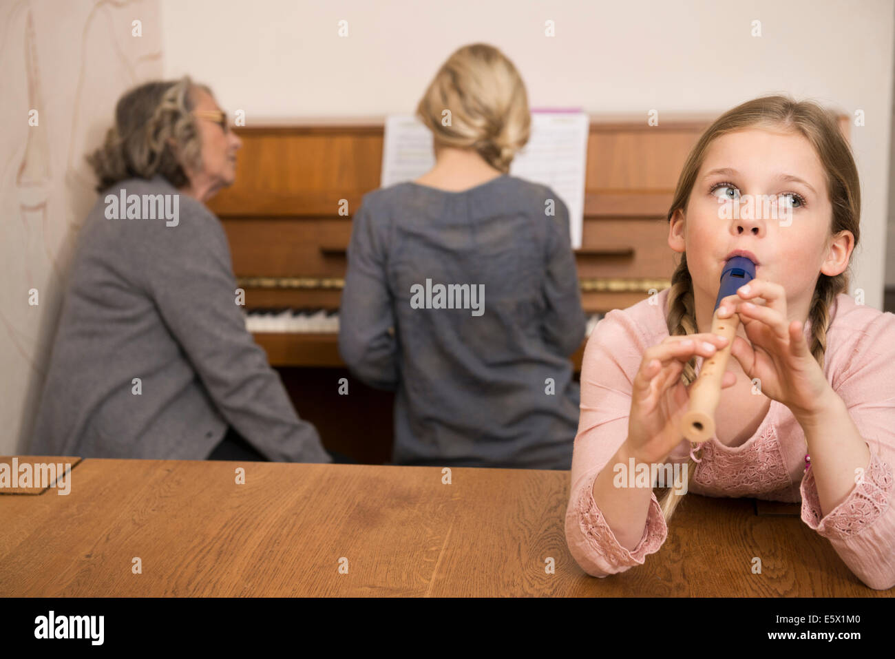 Girl playing recorder while sister on piano watched by grandmother ...
