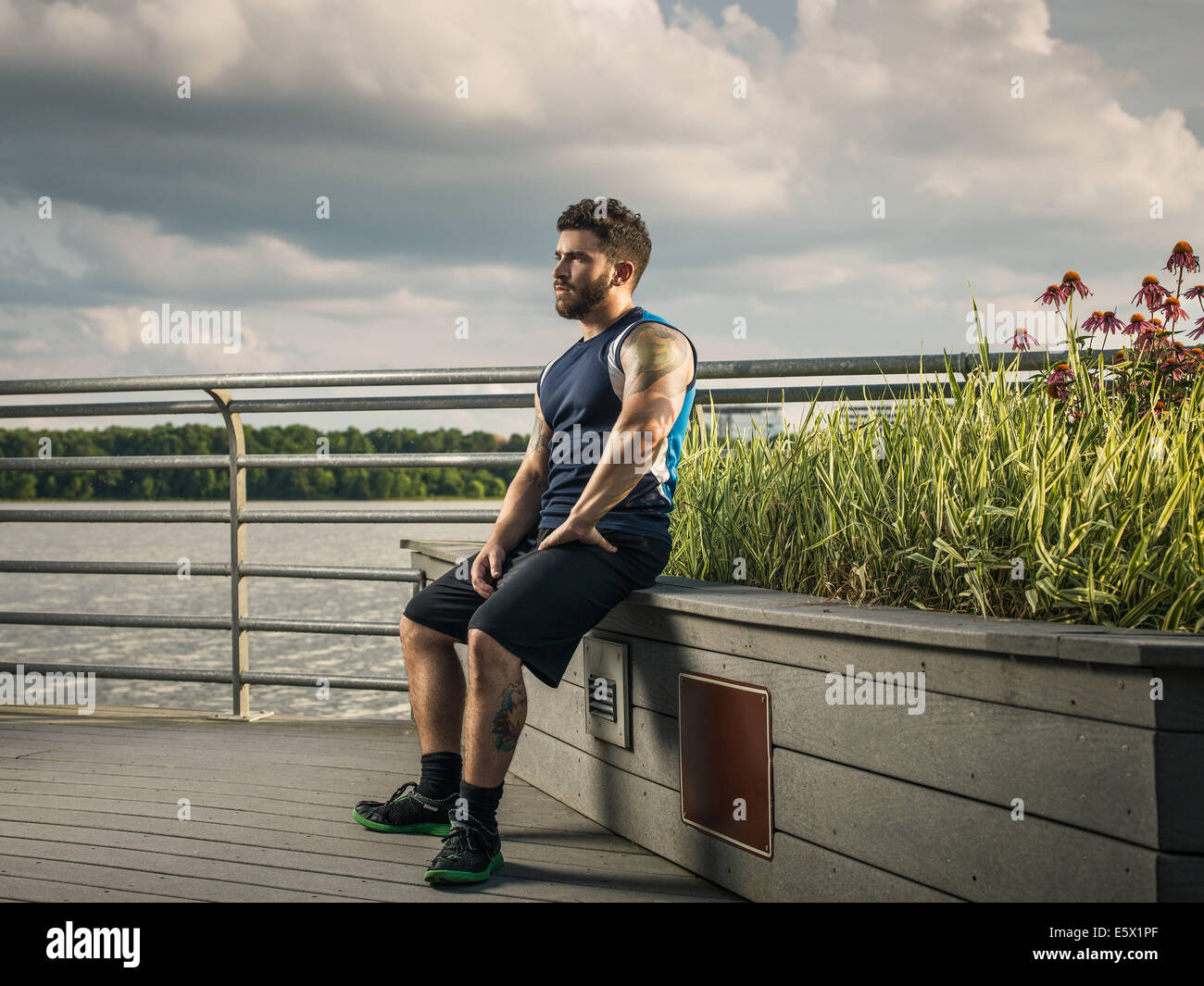 Young man taking a break from training on lake pier seat Stock Photo ...