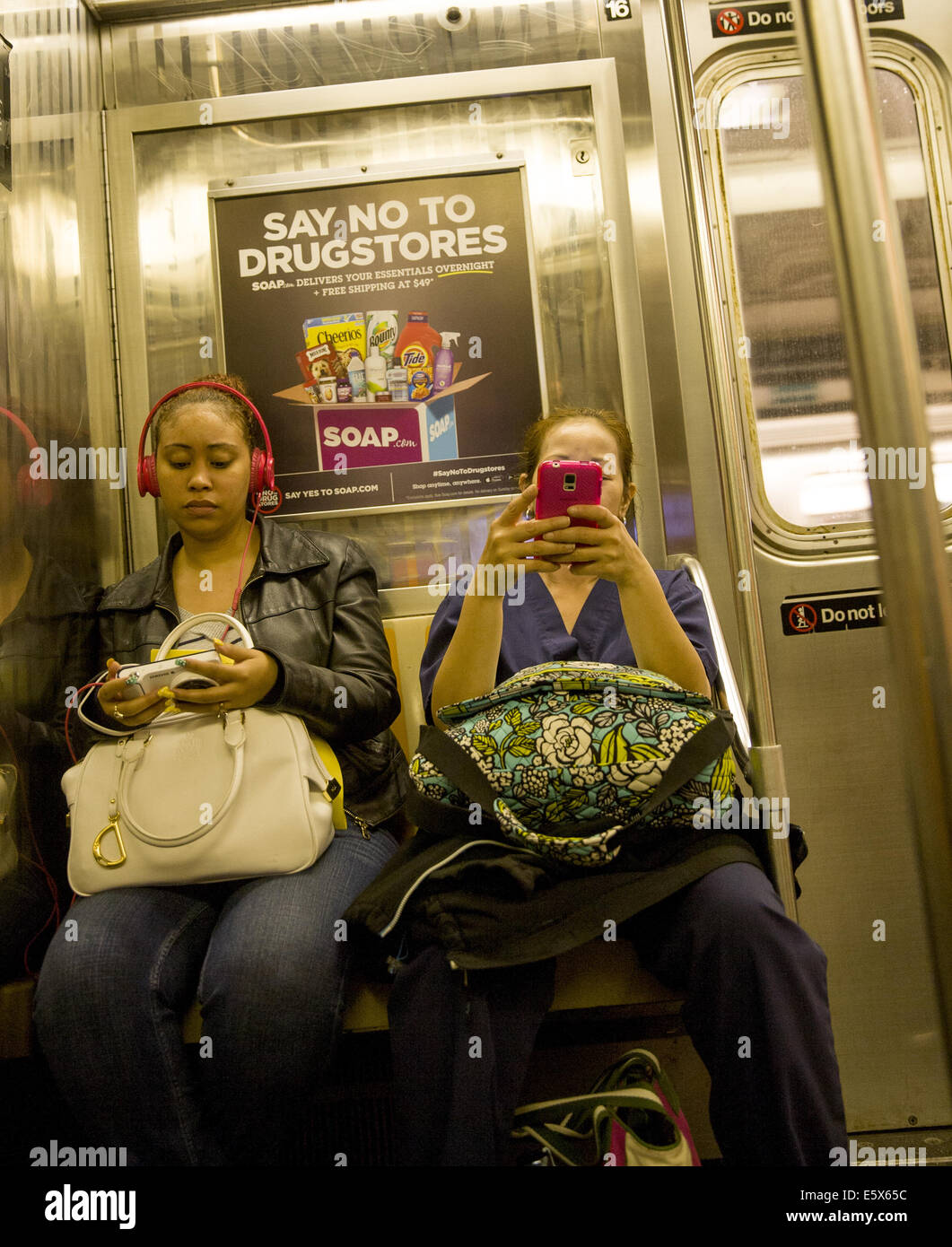 People use their electronic devices on a New York City subway train ...