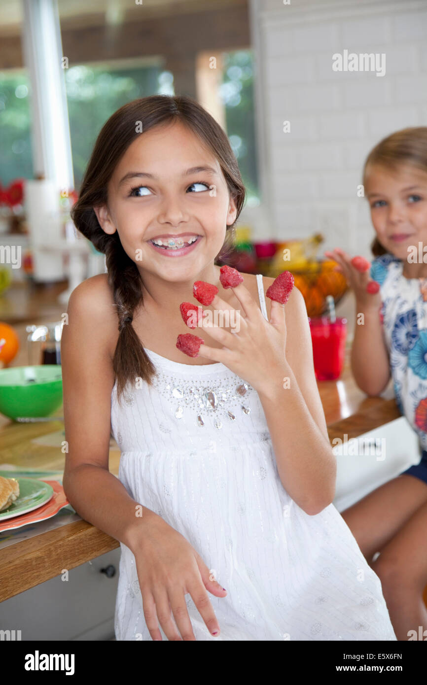 Two mischievous sisters with raspberries on their fingers in kitchen ...