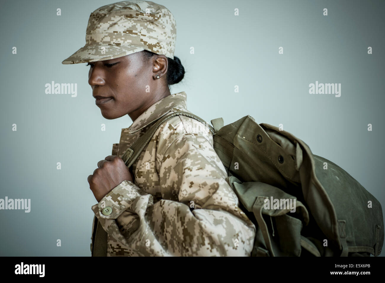 Side view studio portrait of female soldier with rucksack looking down ...