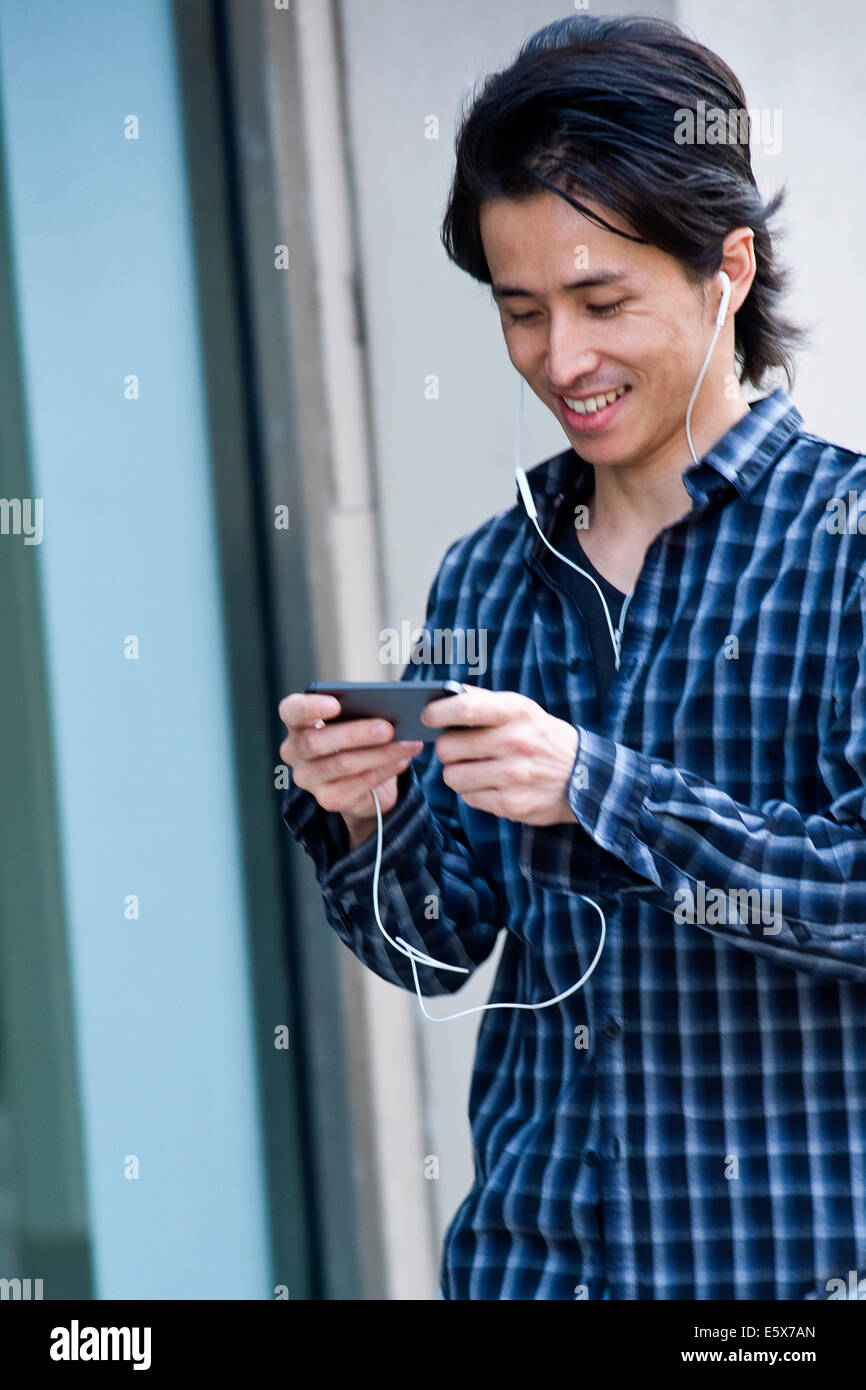 Mid adult man walking down city street selecting music on smartphone ...