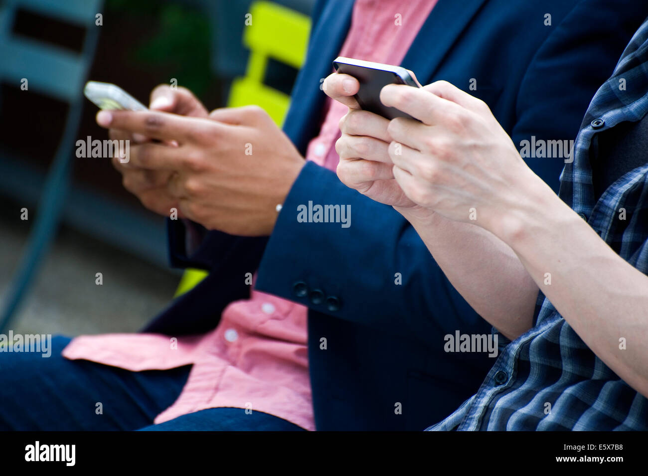 Cropped torso shot of young businessmen in city park texting on ...