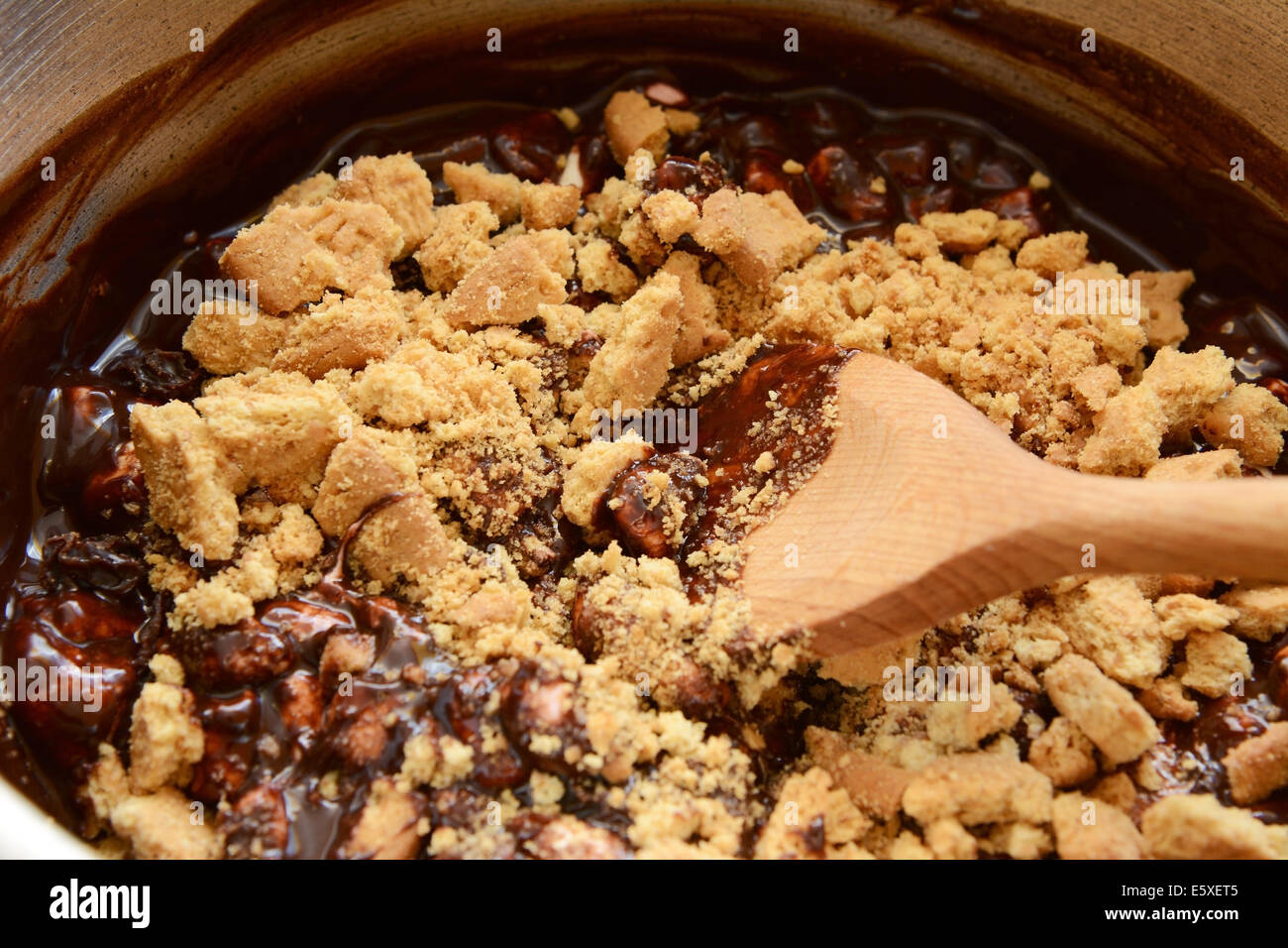 Stirring crushed digestive biscuits into melted chocolate with a wooden ...