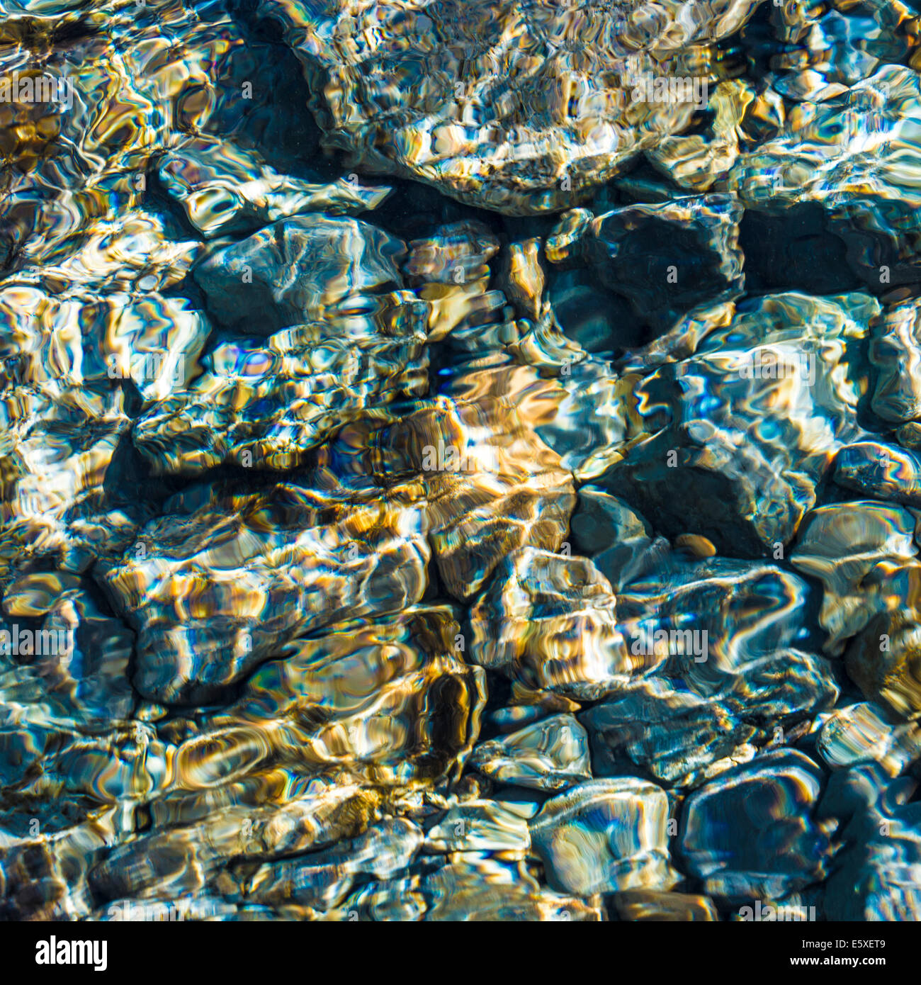 Abstract colourful shallow water ripple patterns above sunlit pebbles ...