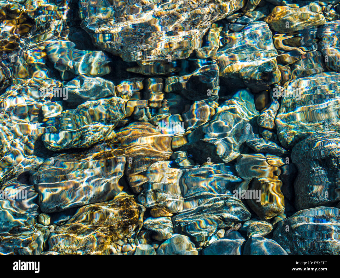 Abstract colourful shallow water ripple patterns above sunlit pebbles ...