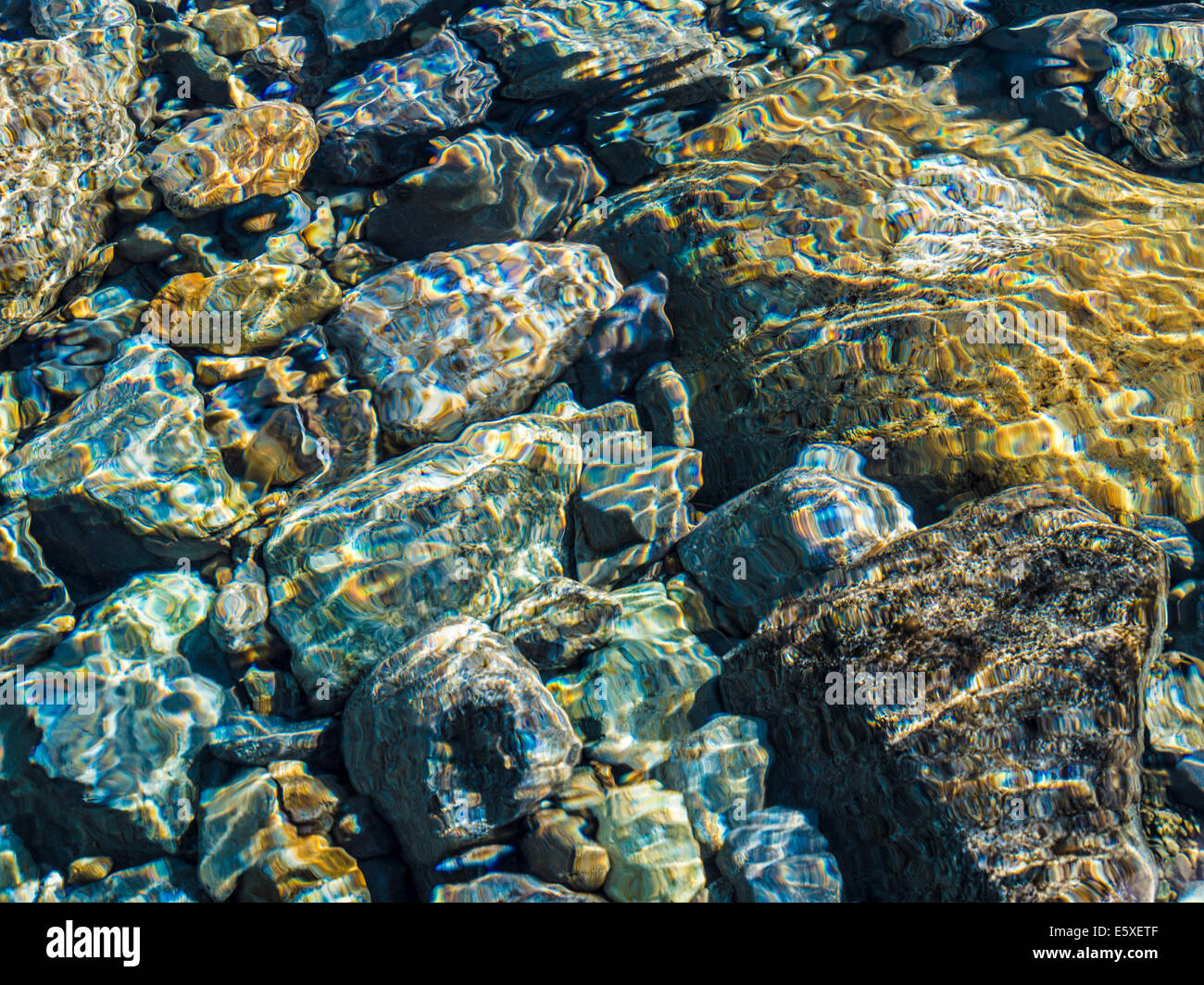 Abstract colourful shallow water ripple patterns above sunlit pebbles ...