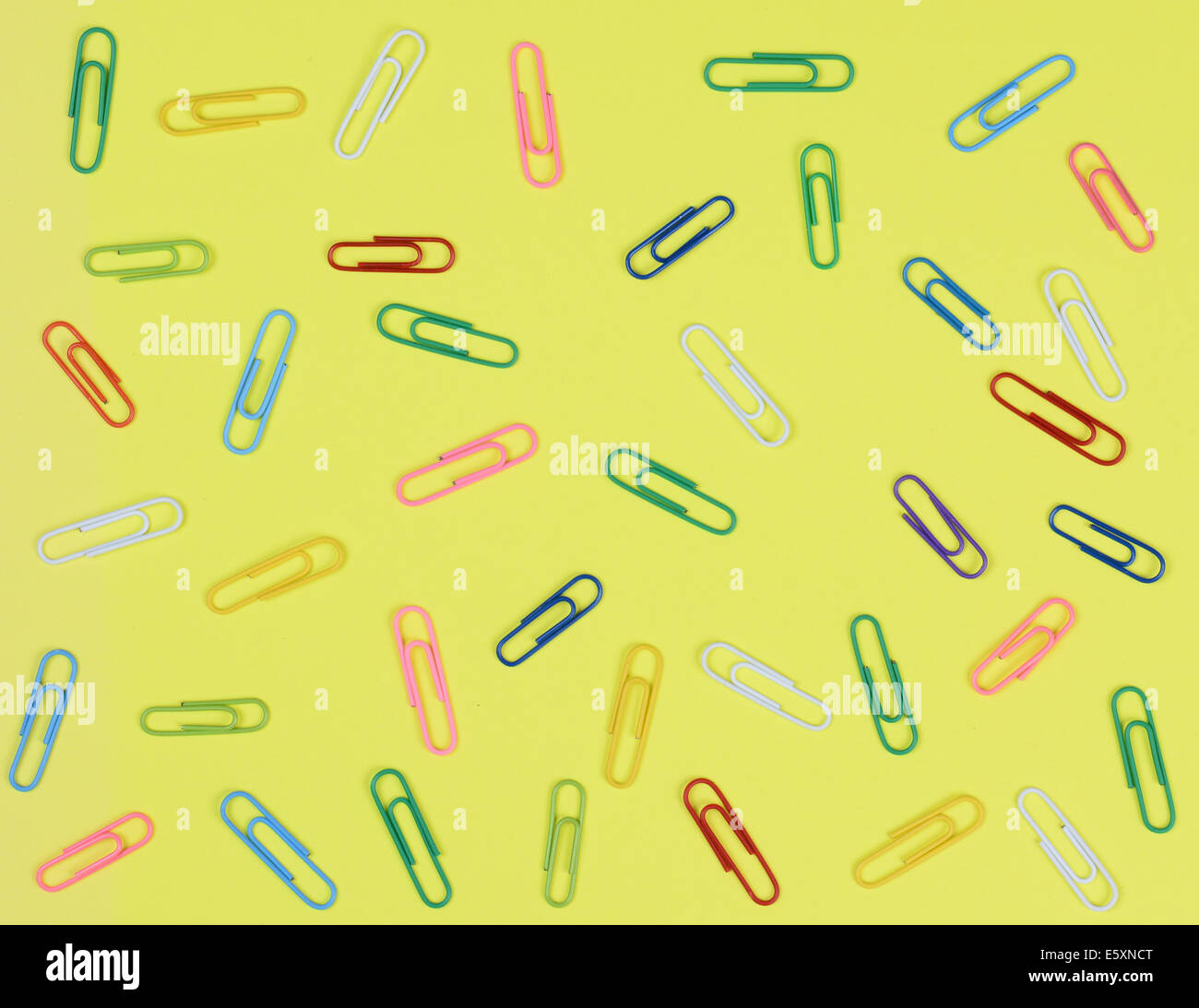 A group of multi-colored paper clips spread out on a yellow background ...