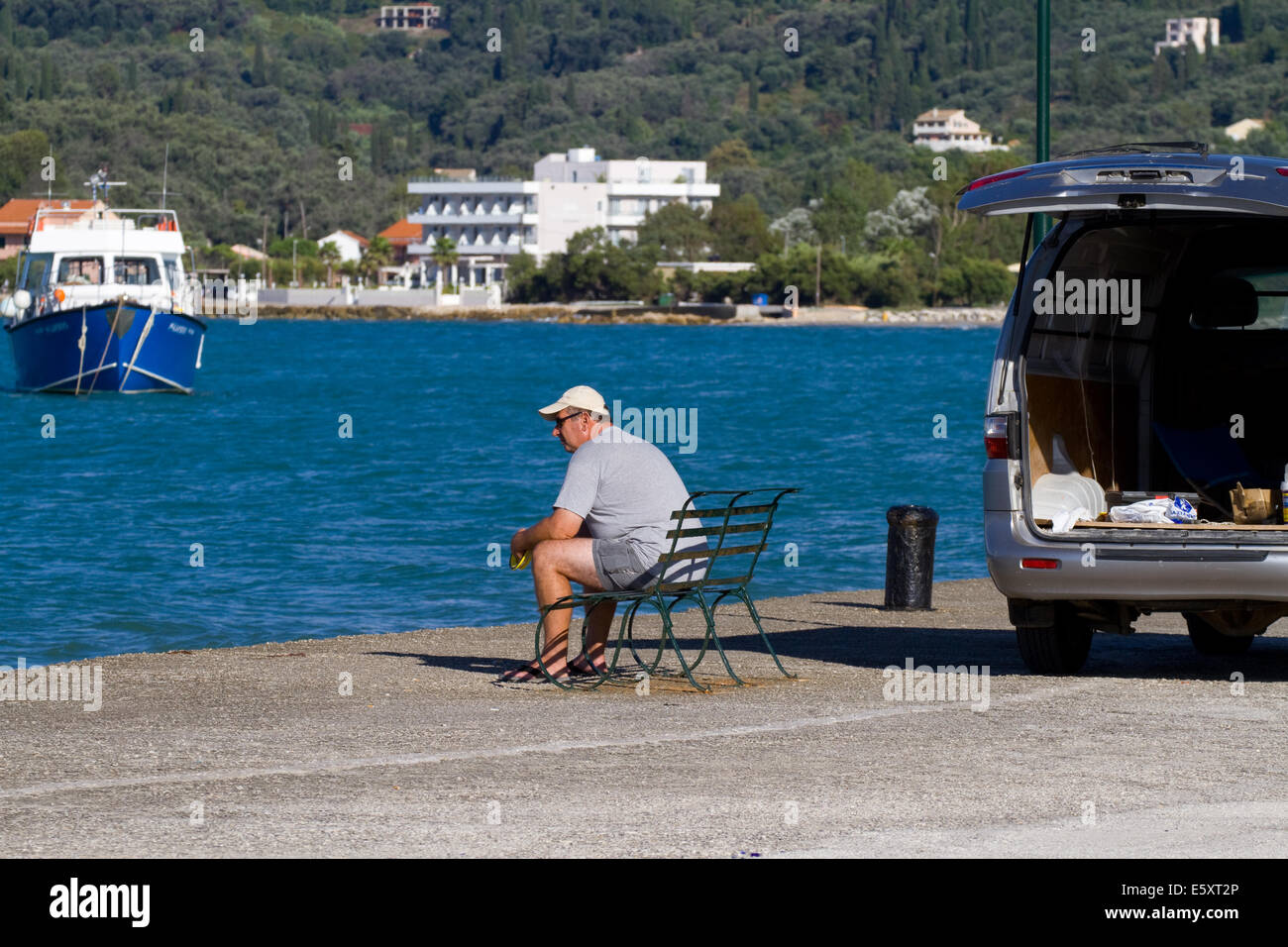Man sitting on bench fishing by handline in harbour. Corfu Stock Photo ...