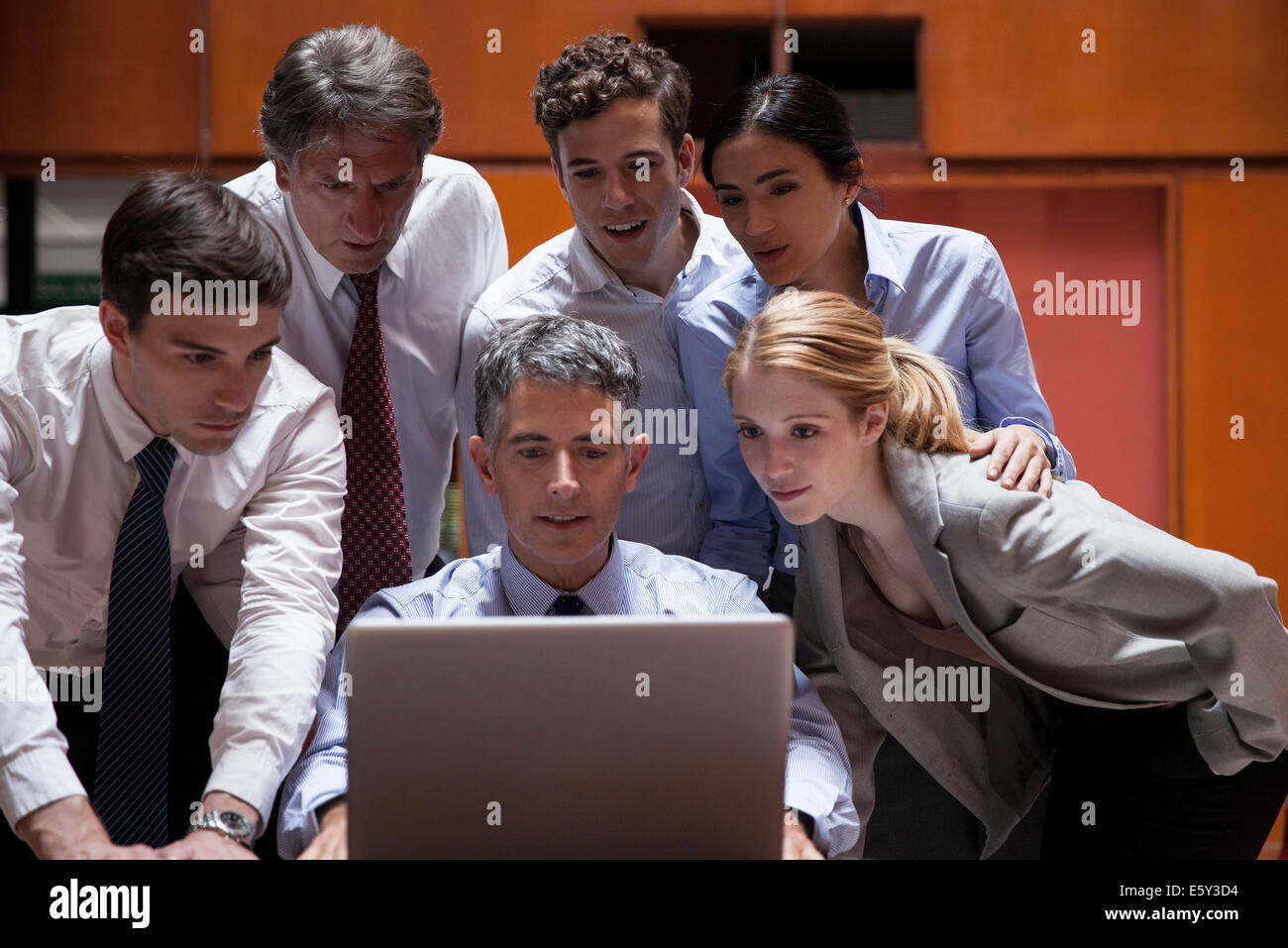 Business associates crowd around colleague looking over his shoulder at ...