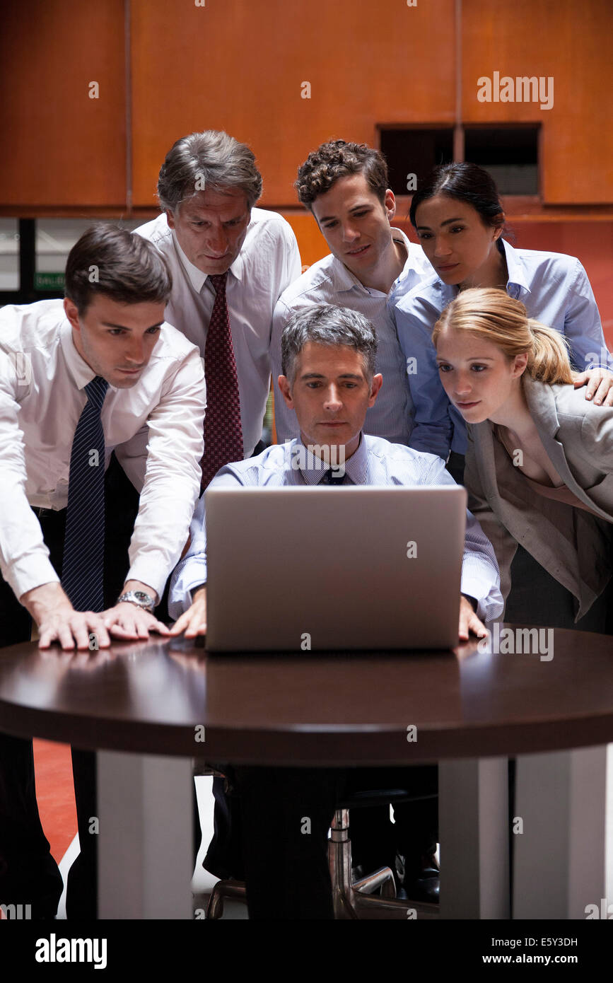 Business associates crowd around colleague looking over his shoulder at ...