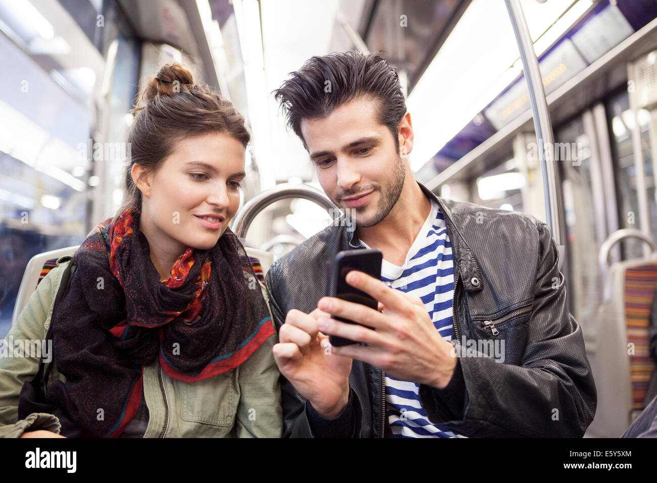 Friends riding subway looking at smartphone together Stock Photo - Alamy