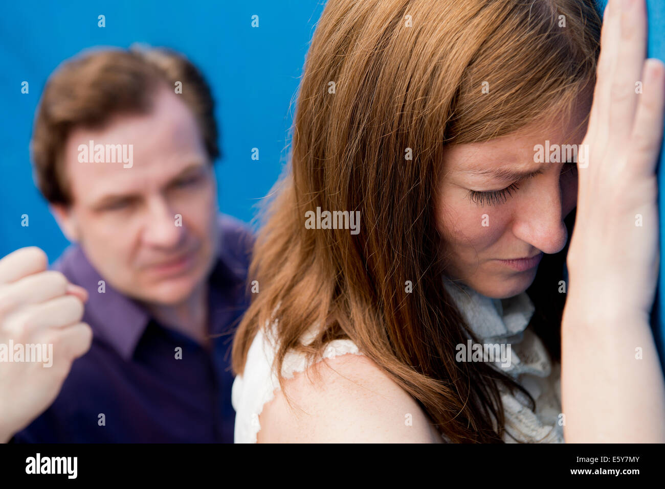 Tearful woman with her back to an aggressive man waving a clenched fist ...