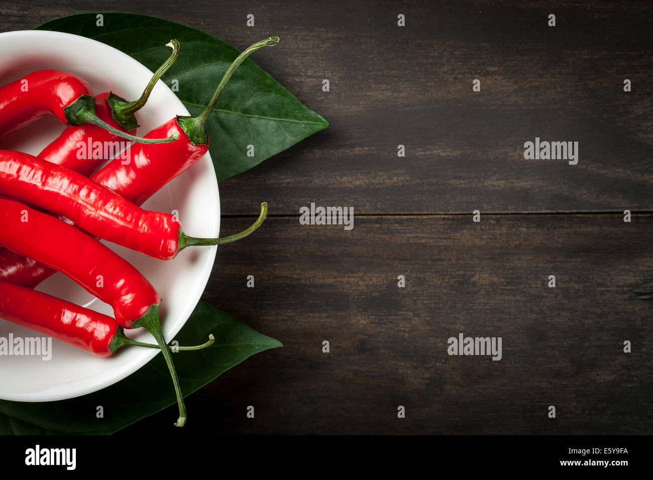 Hot chili peppers on white plate on wooden table background with copy ...