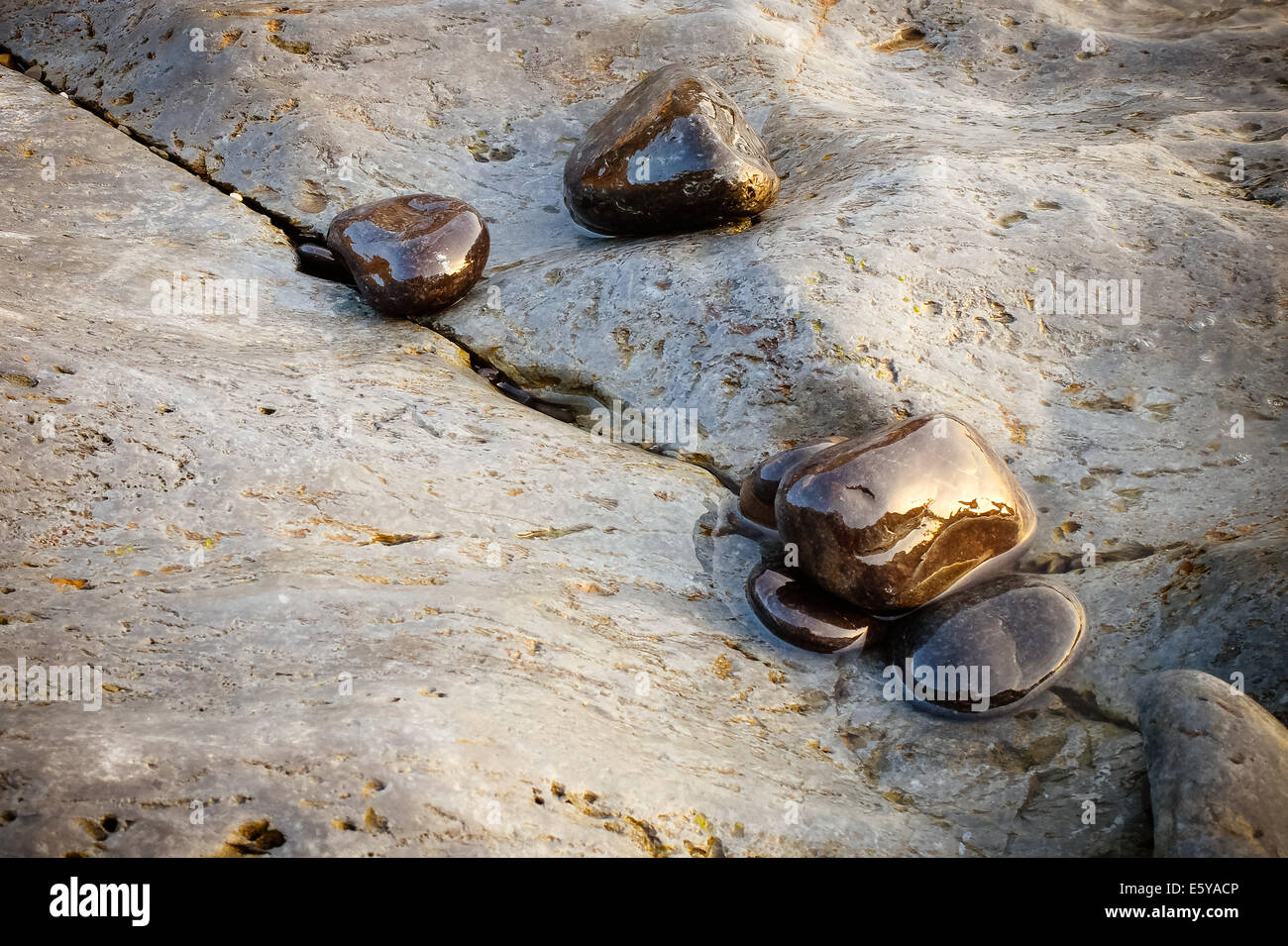 Some beautiful wet stones stand on a big rock near the sea, on a beach ...