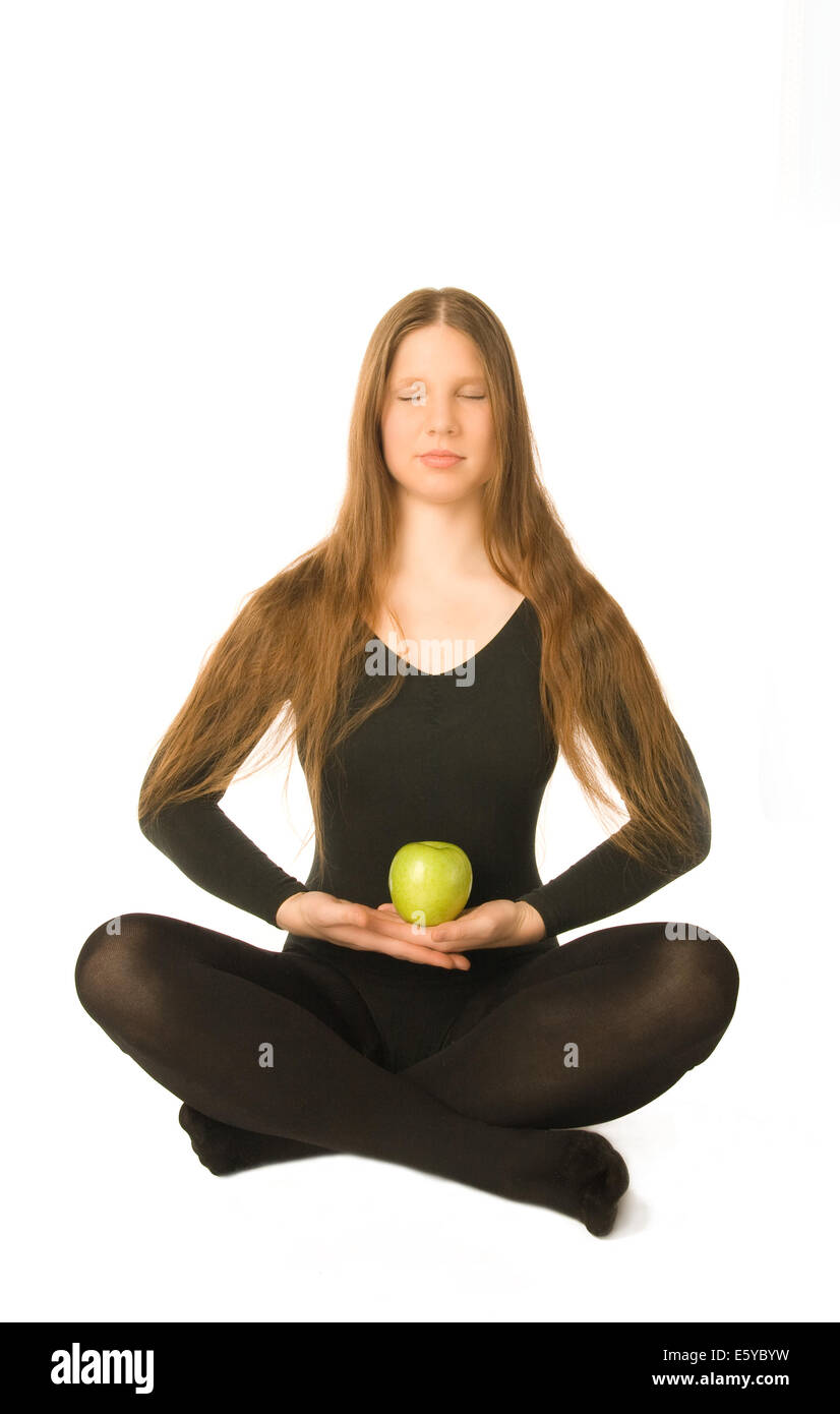 The portrait of a woman in lotus pose with a green apple in her hands ...