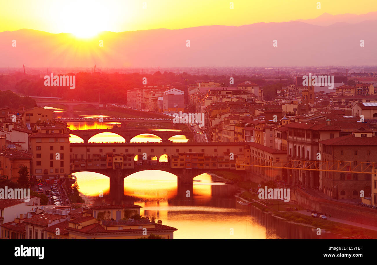 Ancient Italian bridge across Arno river in bright yellow sunset light ...