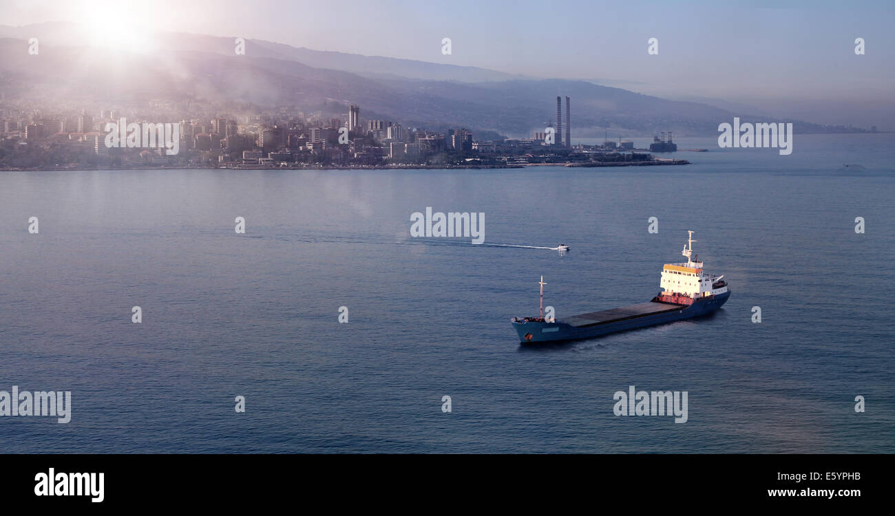 A cargo ship floating on water facing a bay during sunrise, in Lebanon ...