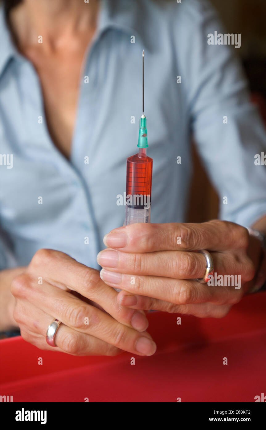 Woman preparing a syringe with a vitamin B solution for herself which ...