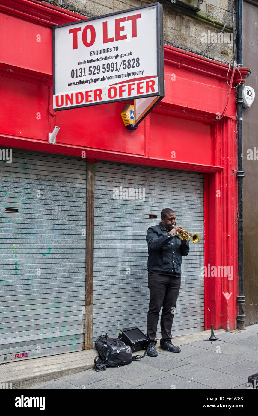 A jazz musician busking beneath a "To Let" sign outside a shop on ...