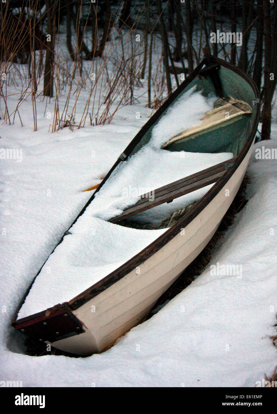 A rowing boat laying askew on a snow covered beach partly filled with ...